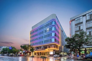 Um hotel com vários andares e design moderno, com um logotipo em formato de H bem visível na fachada.