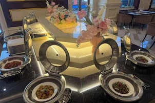Disposição de buffet com várias estações de serviço, incluindo recipientes com comida e um arranjo floral central.
