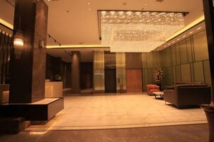 Um hall amplo com um grande candelabro, um balcão de recepção e uma área de estar com um sofá e poltronas.