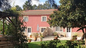 Um edifício vermelho com telhado em telhas, paredes de pedra e um pátio com mobiliário de exterior.
