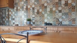 Uma cozinha com painel de azulejos, armários de madeira, pia e mesa de jantar com cadeiras.