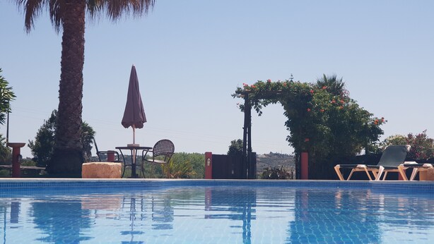Piscina azul cristalina com espreguiçadeiras e mesa com guarda-sol.