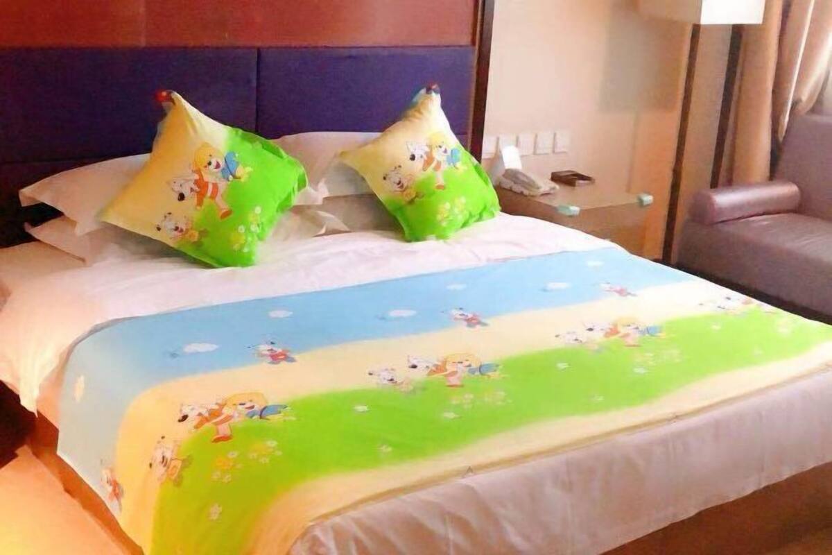 Cama com colcha de tema praiano, dois travesseiros com personagens de desenho animado, mesa de cabeceira com abajur e uma cadeira.