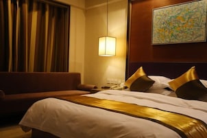 Quarto de hotel com cama, sofá, luminária e um quadro na parede.