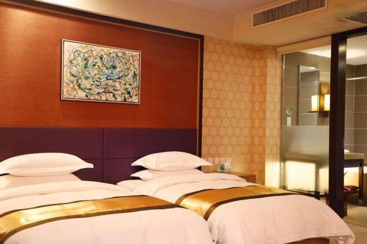 Quarto de hotel com duas camas, um quadro abstrato grande na parede e um banheiro com espelho e pia.