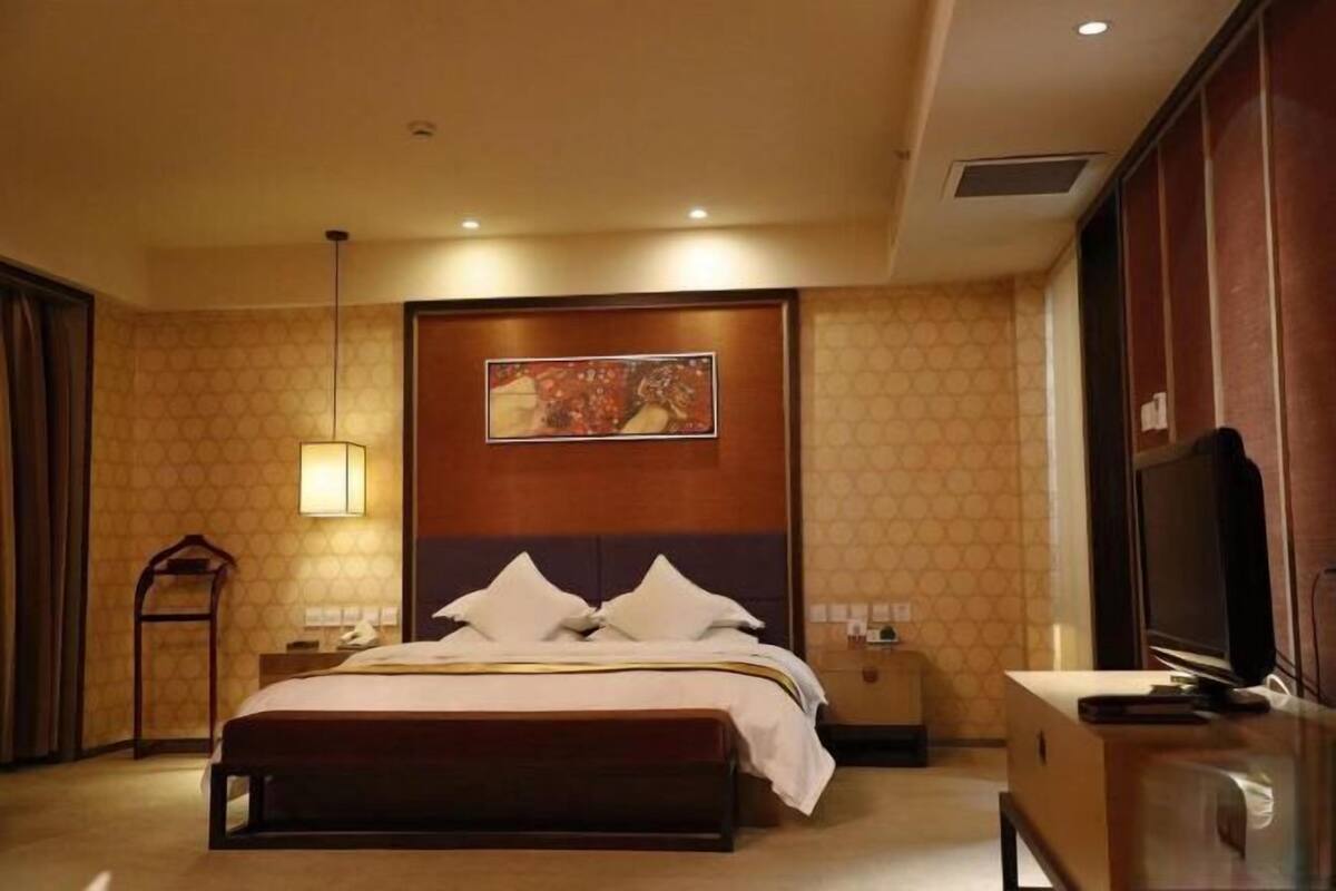 Quarto de hotel com cama, mesas de cabeceira, televisão e um quadro na parede.