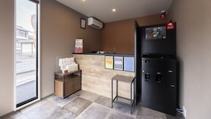 Quarto de hotel com porta de correr para o exterior, uma pequena mesa e cadeira, um frigorífico preto e um armário de madeira.