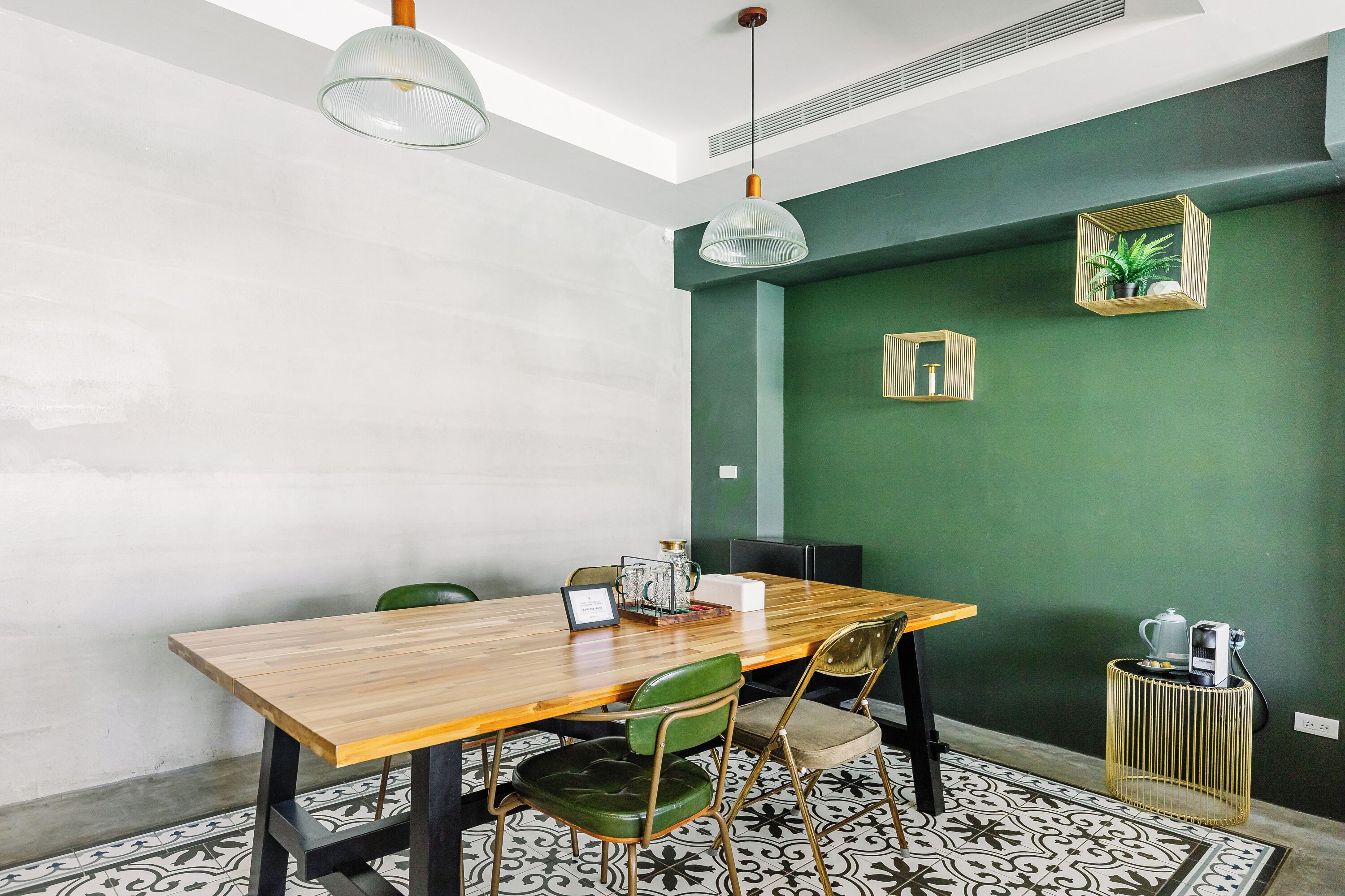 Uma área de refeições com mesa de madeira, cadeiras verdes e um tapete estampado.