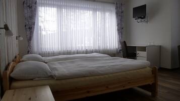 Quarto com duas camas de solteiro, uma escrivaninha, uma cadeira e televisão fixada na parede.