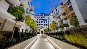 Um edifício de apartamentos moderno com um pátio central, rodeado por árvores e caminhos iluminados.
