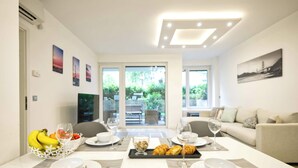 Uma área de refeições com uma mesa posta para dois, com pratos, talheres e uma cesta de frutas.