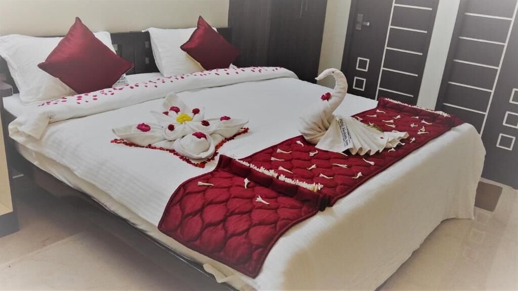 Cama bem arrumada com lençóis brancos, almofadas vermelhas e brancas e almofadas decorativas em formato de cisne.