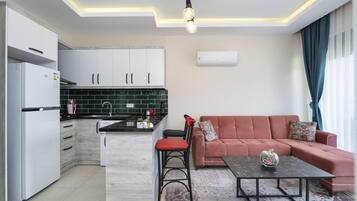Uma cozinha moderna com armários brancos, bancada preta e uma cadeira vermelha. Há um sofá com almofadas estampadas e uma mesa de centro com um objeto decorativo.