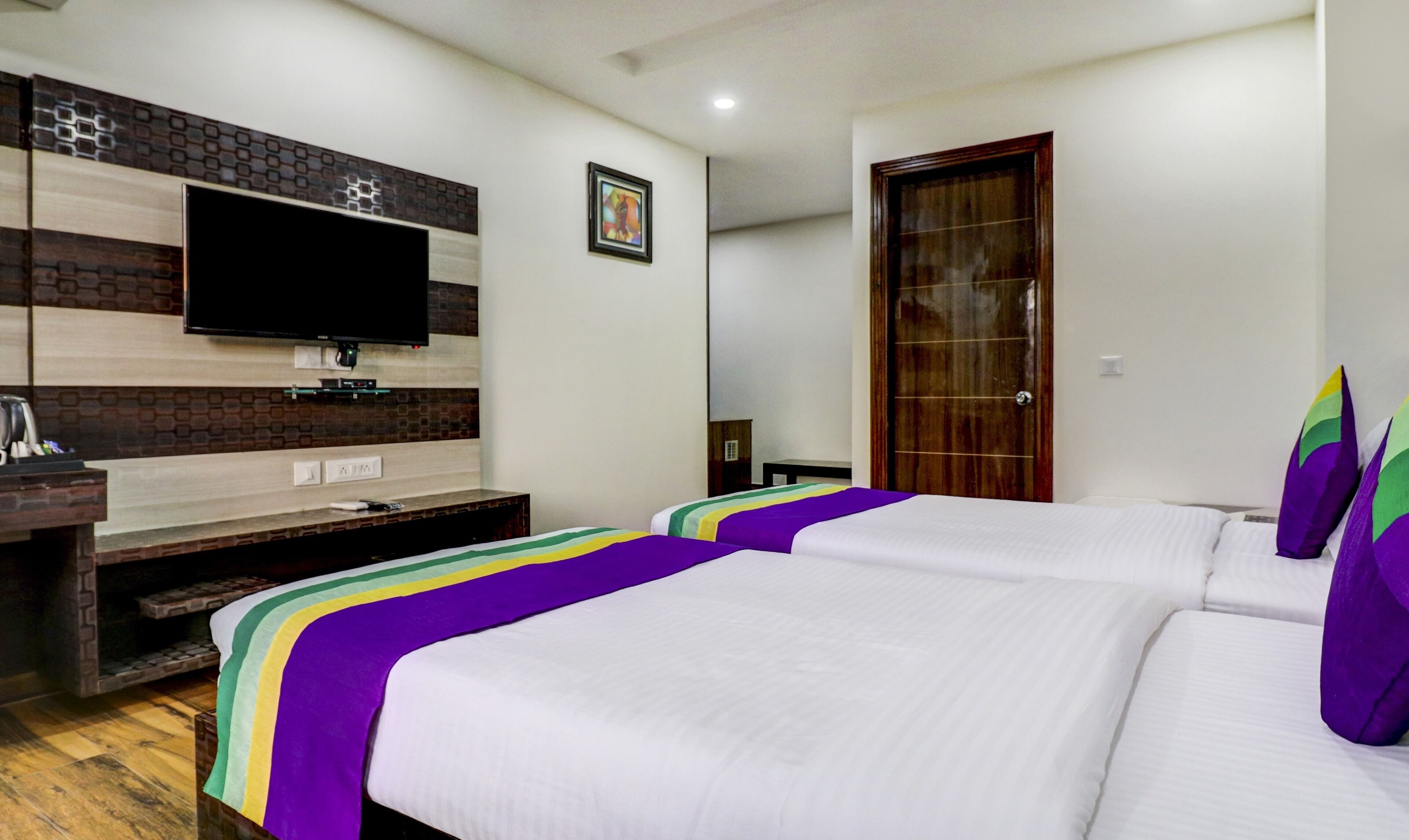 Quarto de hotel com duas camas, uma televisão fixada na parede, um armário de madeira e uma porta com espelho.