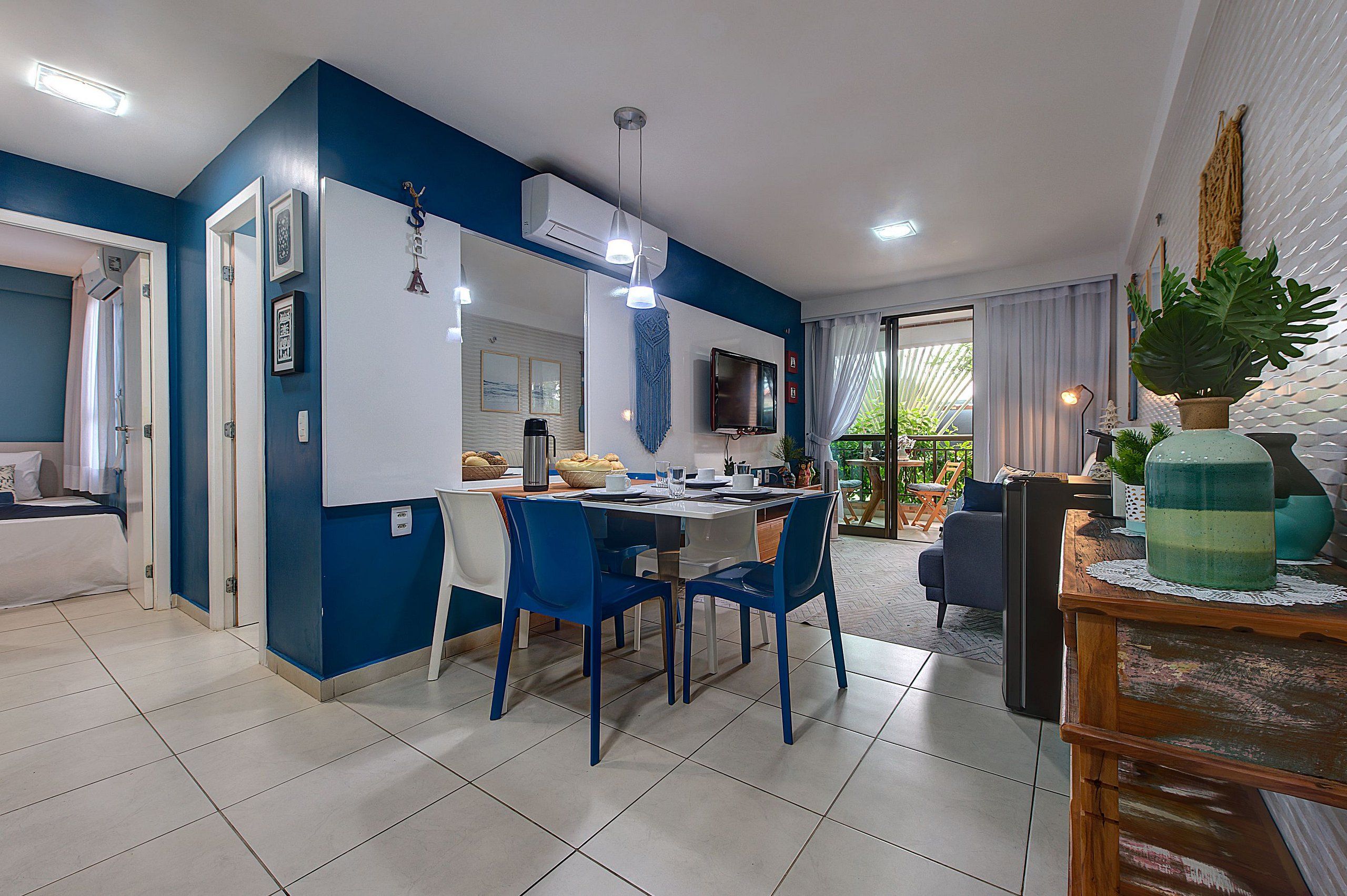 Cozinha moderna com detalhes em azul, área de jantar com cadeiras azuis e uma janela ampla com vista para um jardim.