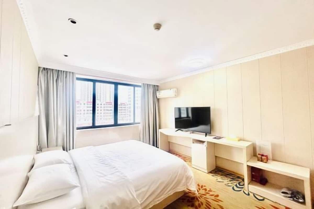 Quarto de hotel com cama, televisão, secretária e janela com cortinas.