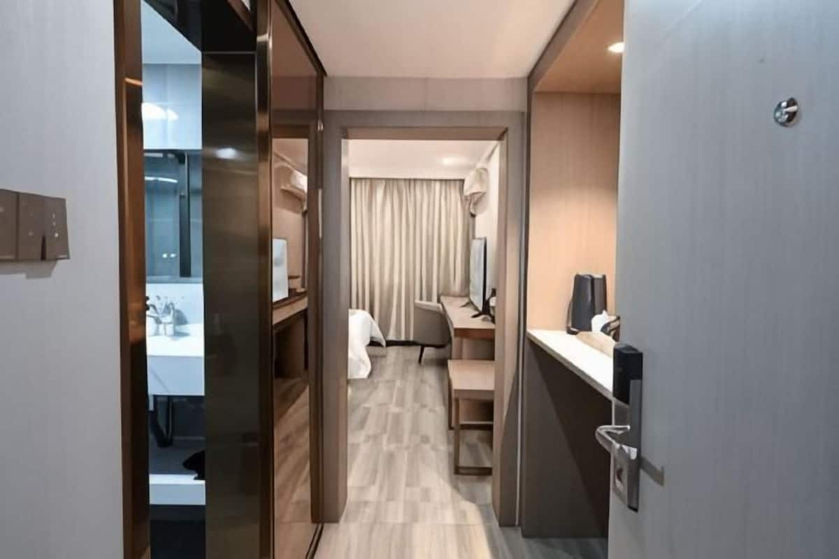 Corredor estreito que leva a um quarto com escrivaninha, cadeira e cama.