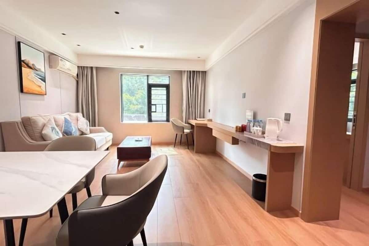 Quarto de hotel moderno com sofá, mesa de jantar, cadeiras, pequena cozinha e uma janela grande.