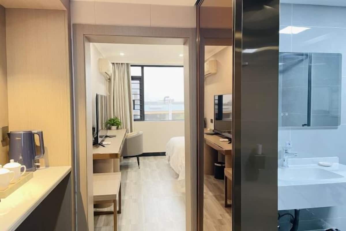 Quarto de hotel com cama, escrivaninha, televisão e banheiro com pia e espelho.