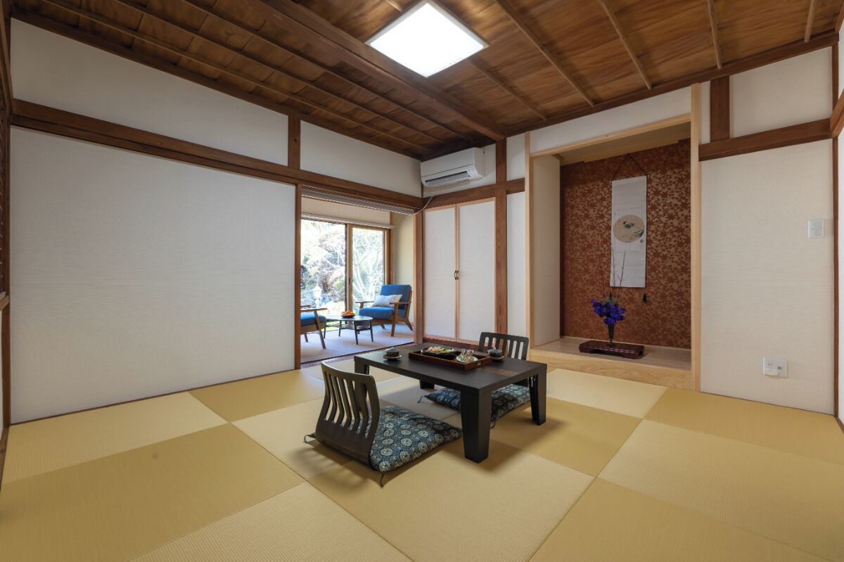 Um quarto japonês tradicional com tatames, uma mesa baixa com almofadas e uma porta deslizante que dá para uma área externa.