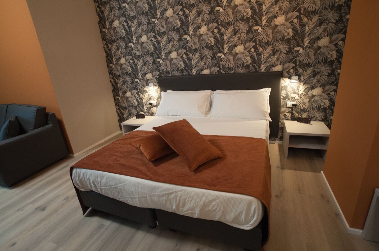 Quarto com cama, duas mesas de cabeceira, um criado-mudo, um sofá e papel de parede floral.
