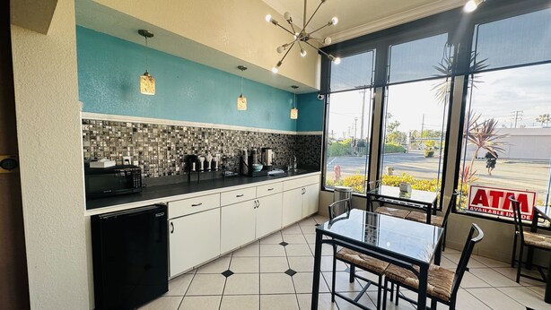 Uma cozinha moderna com bancada preta, armários brancos e piso ladrilhado. Há um espaço de refeições com mesa de vidro e cadeiras.