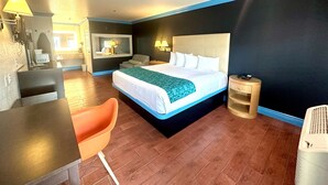 Quarto de hotel com uma cama grande, uma escrivaninha, uma cadeira, um espelho e uma mesinha.