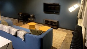 Uma sala de estar moderna com um sofá azul, duas mesas laterais amarelas, uma TV de tela plana fixada na parede e um pequeno móvel de madeira para a TV.