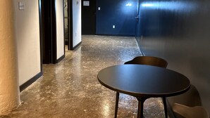 Um corredor com uma mesa redonda e cadeiras, uma porta e uma parede escura.