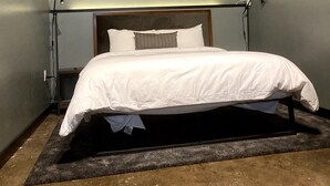 Quarto com cama, cabeceira, luminárias laterais e piso coberto por carpete.