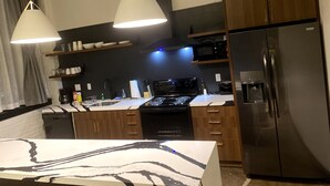 Uma cozinha moderna com ilha central, eletrodomésticos de aço inoxidável, armários de madeira e iluminação pendente.