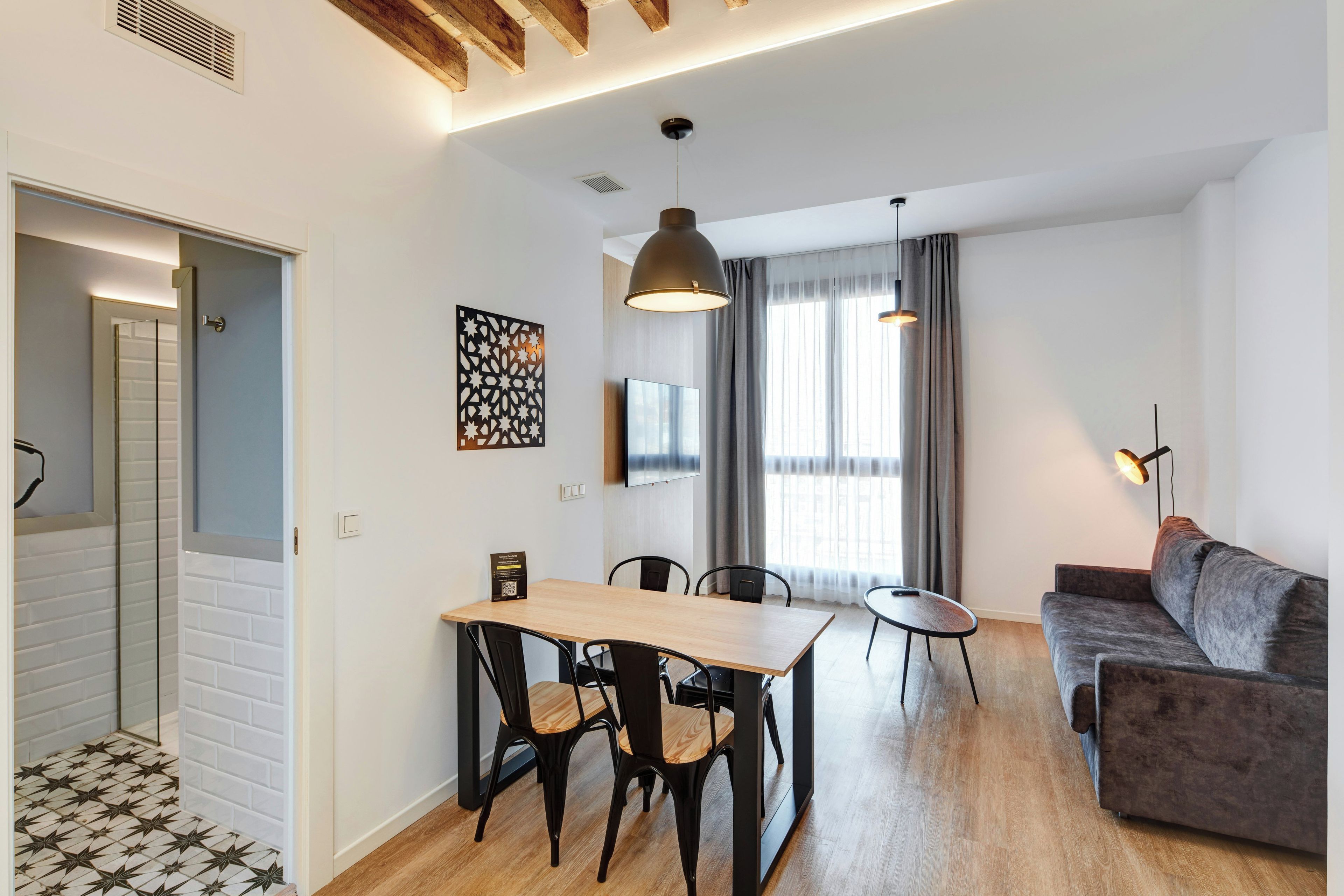 Uma sala de estar moderna com um sofá, uma mesa de jantar com cadeiras e uma TV fixada na parede.
