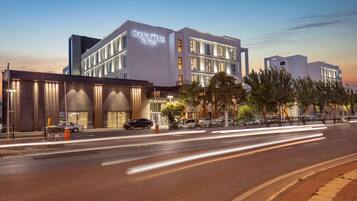 Um hotel moderno com uma placa em destaque indicando "DOUBLETREE by Hilton", apresentando uma estrutura em vários andares com grandes janelas e fachada bem iluminada.