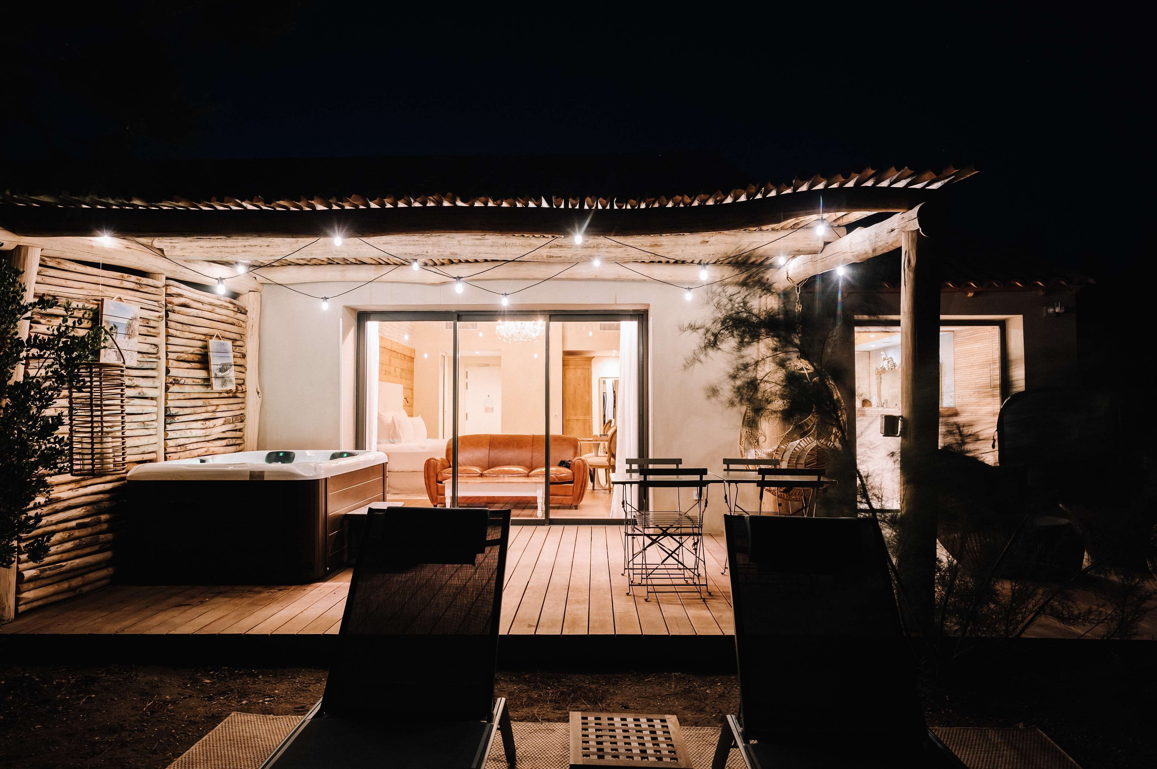 Um pátio externo acolhedor com hidromassagem, área de estar e entrada coberta que dá acesso a um espaço interior bem iluminado.