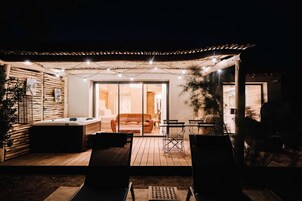 Um pátio externo acolhedor com hidromassagem, área de estar e entrada coberta que dá acesso a um espaço interior bem iluminado.