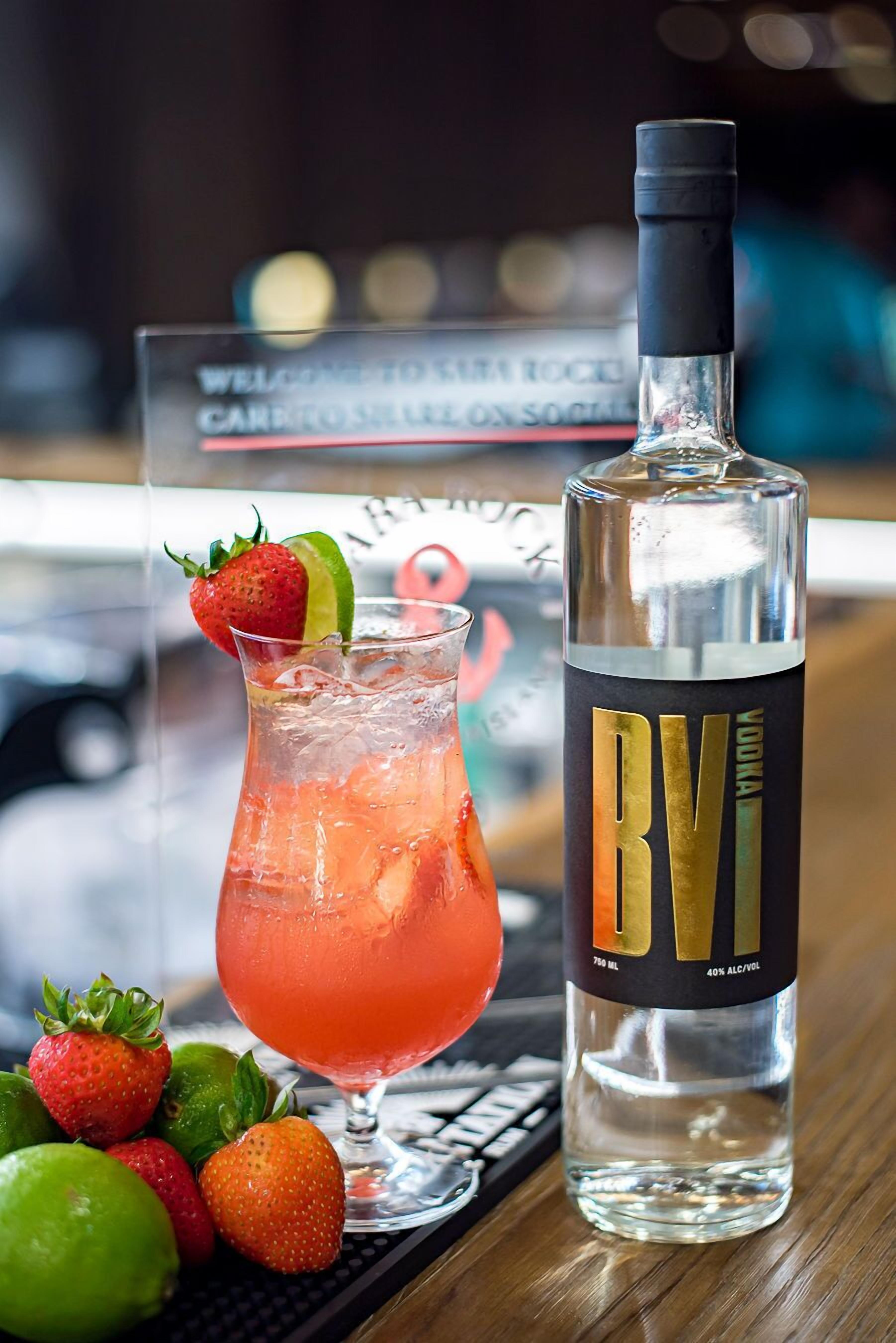 Uma garrafa de vodka BVI e um copo de cocktail com morangos e limão.