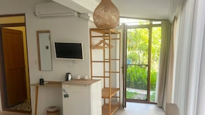 Sala de estar moderna com sofá, televisão, pequeno espaço de cozinha e uma grande janela com vista para área verde.