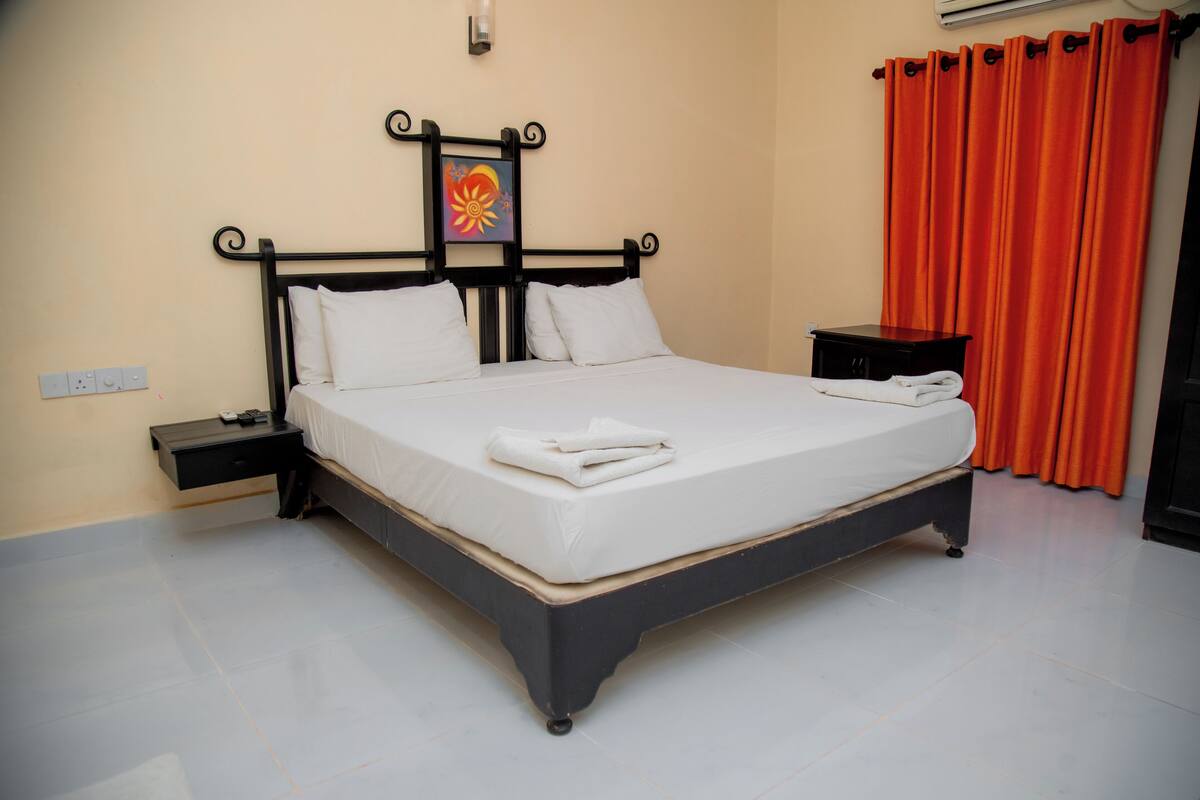 Cama bem arrumada com lençóis brancos, cabeceira preta e uma pequena mesa de cabeceira com uma toalha branca dobrada.
