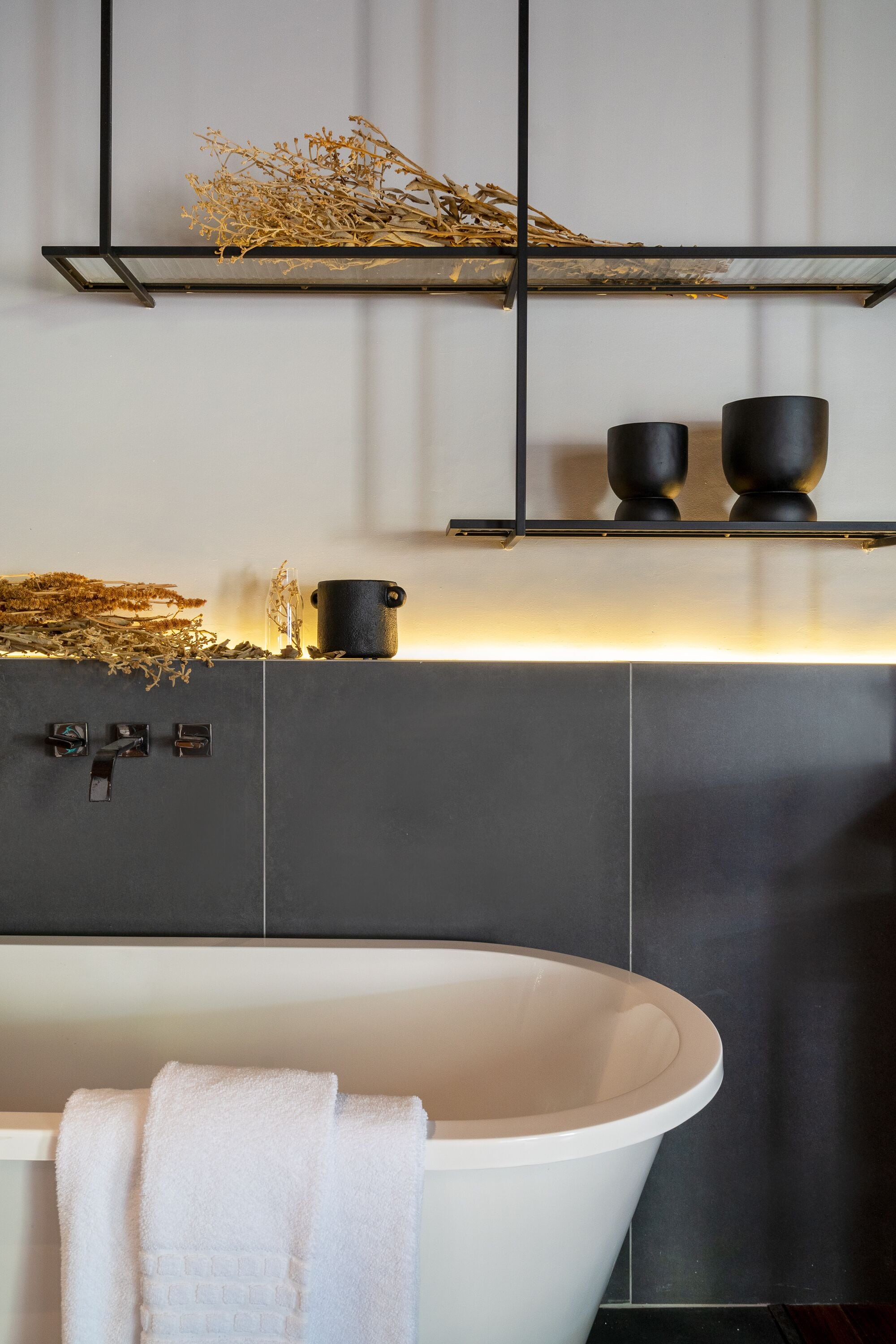 Uma casa de banho moderna com uma banheira independente, um porta-toalhas e uma estante com ramos decorativos e dois recipientes pretos.