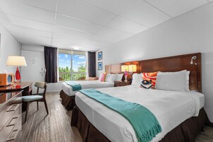Quarto de hotel com duas camas, uma escrivaninha com luminária, uma cadeira e vista para o exterior.