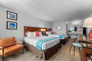 Quarto de hotel com duas camas, uma escrivaninha, uma cadeira e um banheiro visível por uma porta aberta.