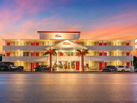 Hotel com vários andares e design retrô, com entrada destacada, cobertura e palmeiras.