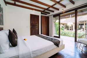 Quarto com cama, vigas de madeira no teto, uma porta e vista para o exterior.