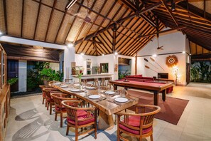 Uma ampla sala de jantar com teto alto e vigas de madeira, mesa de bilhar e um espaço de estar acolhedor com um sofá vermelho.