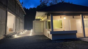 Um edifício moderno com área externa coberta, escadaria que leva a uma porta e parede decorativa com padrão geométrico.