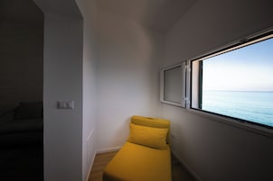 Um quarto pequeno com uma cama de solteiro, uma janela com vista para o mar e um interruptor de luz na parede.