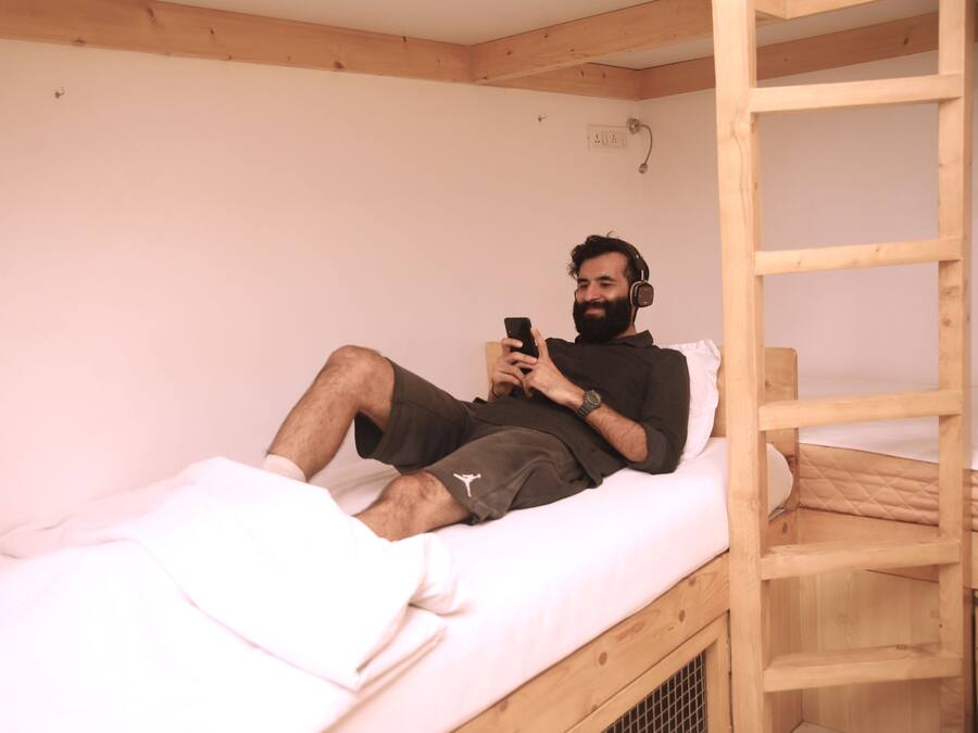 Uma cama beliche com uma pessoa deitada na cama de baixo, usando um smartphone.