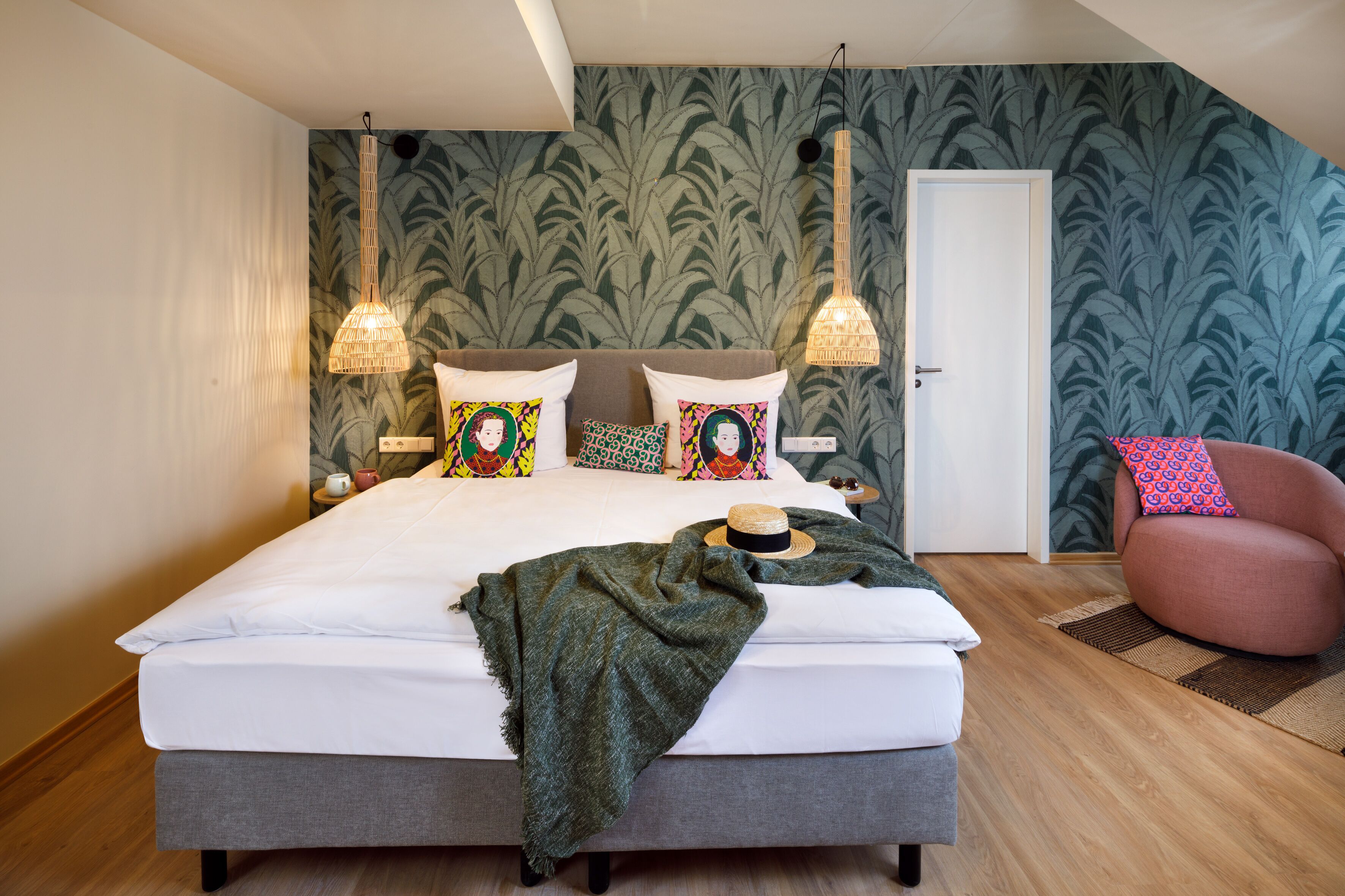 Quarto com uma cama grande, duas luminárias de cabeceira, uma porta e uma cadeira.