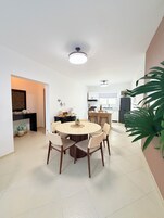Uma cozinha moderna com armários brancos, uma área de refeições com uma mesa redonda e cadeiras, e uma planta verde grande.