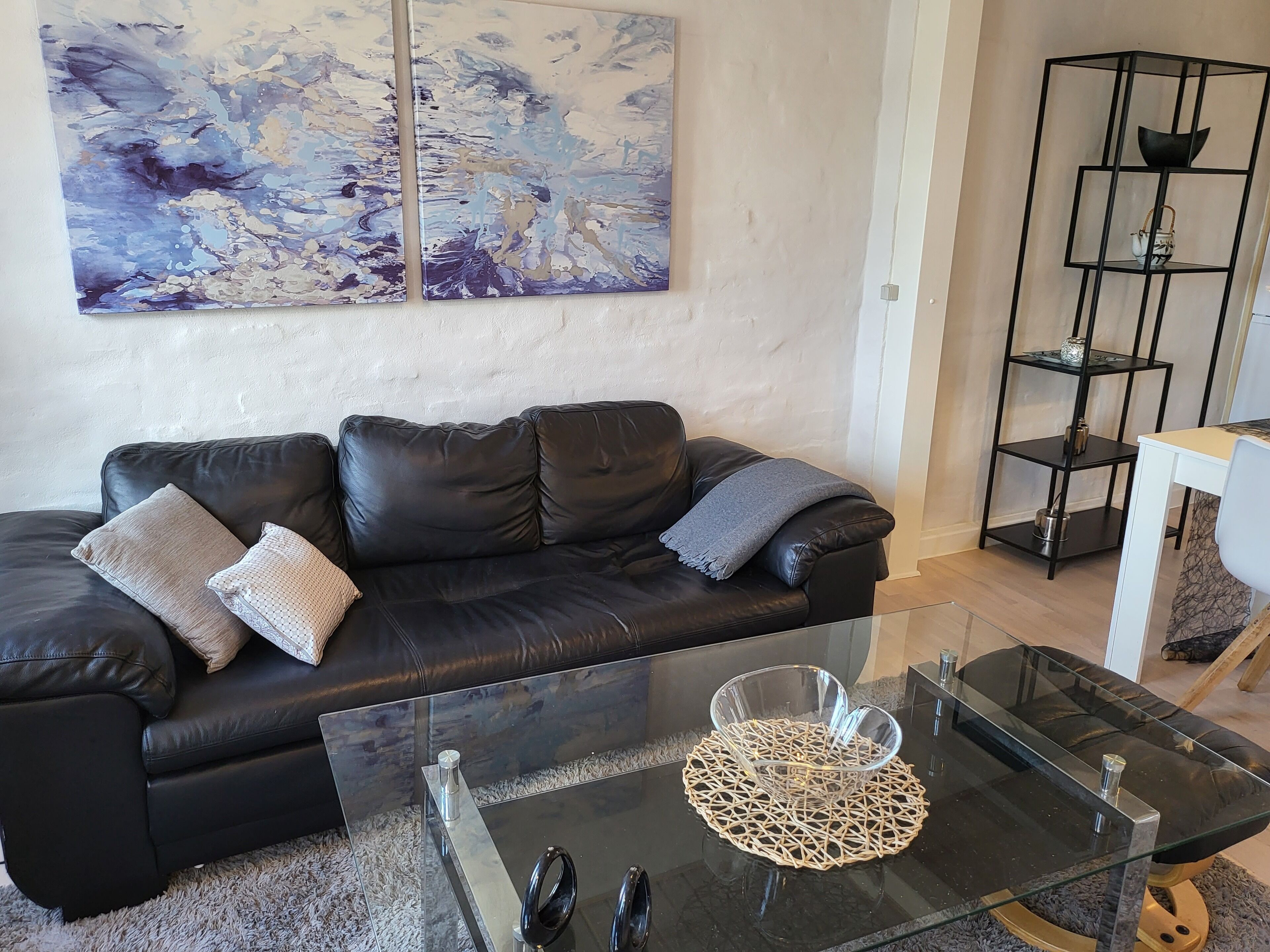 Uma sala de estar moderna com um sofá de couro preto, uma mesa de centro de vidro e uma estante de metal preto.